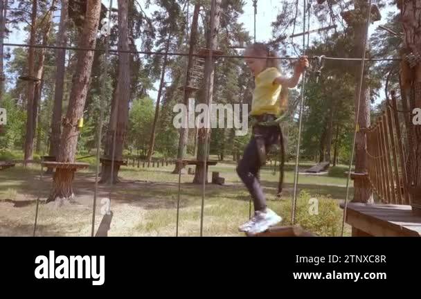 A child in a forest adventure park made of ropes. The girl is climbing ...