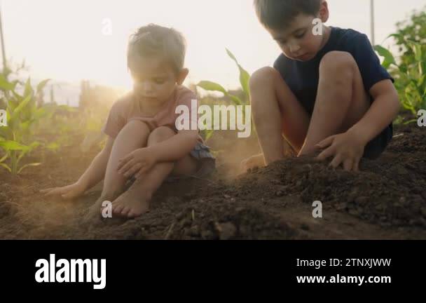 Two adorable children sitting on the ground in the garden, covering ...