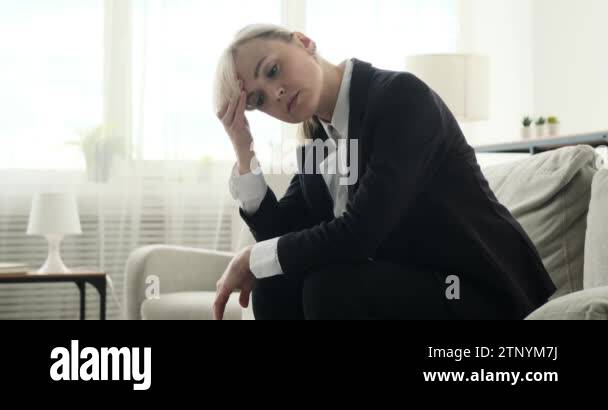 A tired and distressed female entrepreneur sitting on a sofa, visibly ...