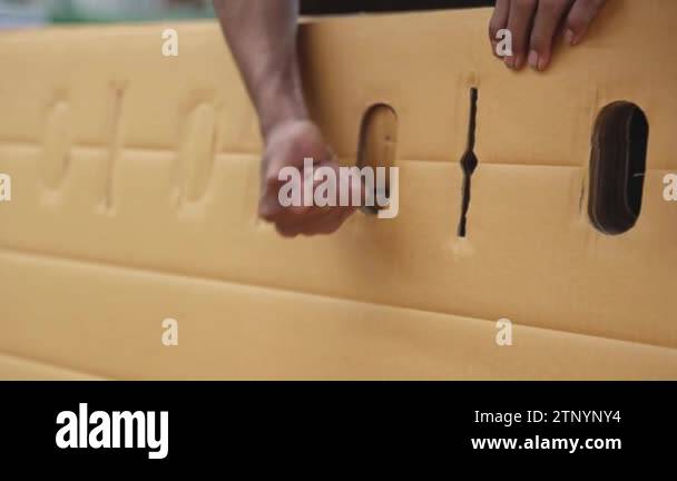 Male worker uses special tool to punch holes in stacked cardboard boxes ...