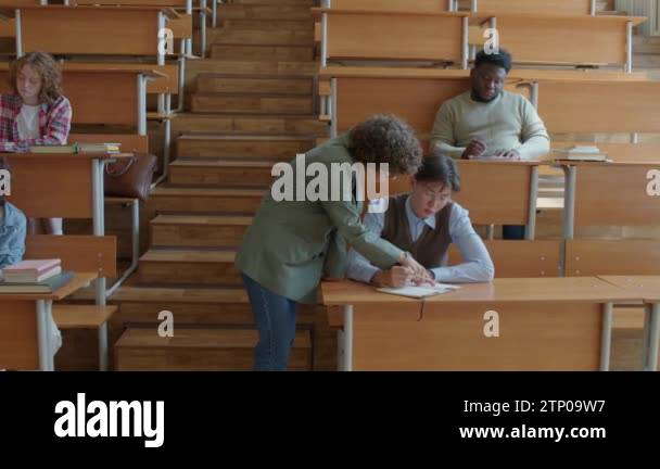 College teacher checking her multi-ethnic students completing task and ...