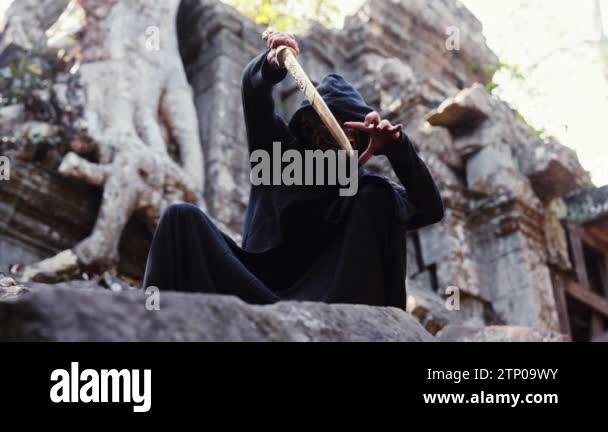 Wide shot of a masked man in black cloak crouched on top of a stone ...