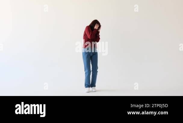 A young Caucasian teenage girl, standing against a clean white backdrop, experiences a sudden ...