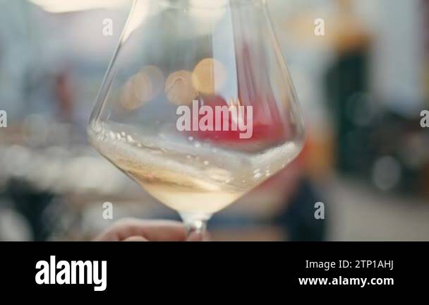 Man hand shaking white wine glass at street bar close up ...