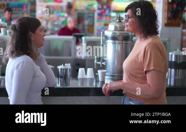 Two women conversing standing at counter inside restaurant cafeteria ...