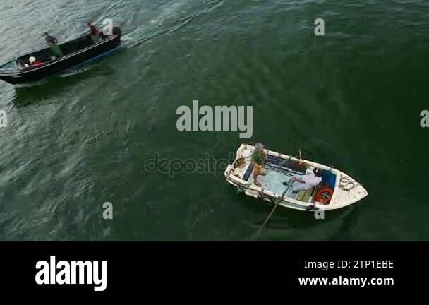 Men sailing in small boat rowing it with oars along river under bridge ...