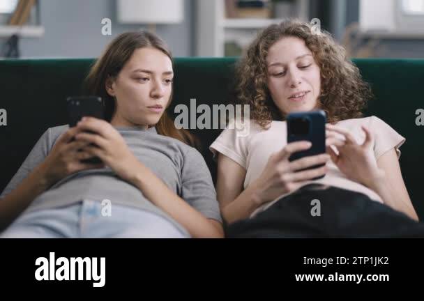 Two cheerful female scrolling on smartphone at home to post on social ...