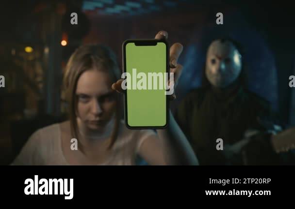 Girl victim of the horror maniac, standing and showing a smartphone and ...