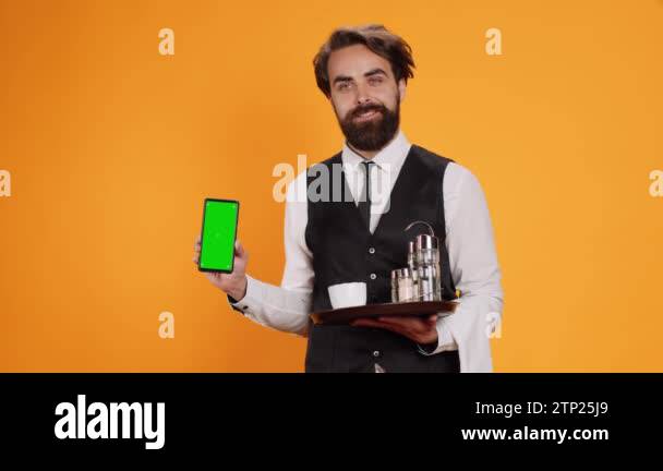 Young waiter shows greenscreen on camera, holding smartphone with blank ...