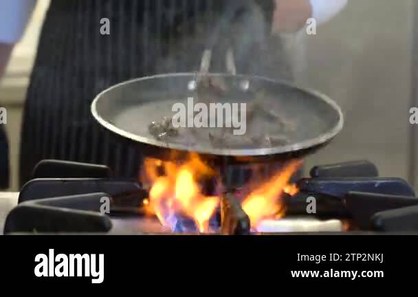 Chef shakes the pan over the stove to cook meat while flames appear ...