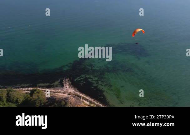 A paraglider soars over the sea and forest with a breathtaking view of ...