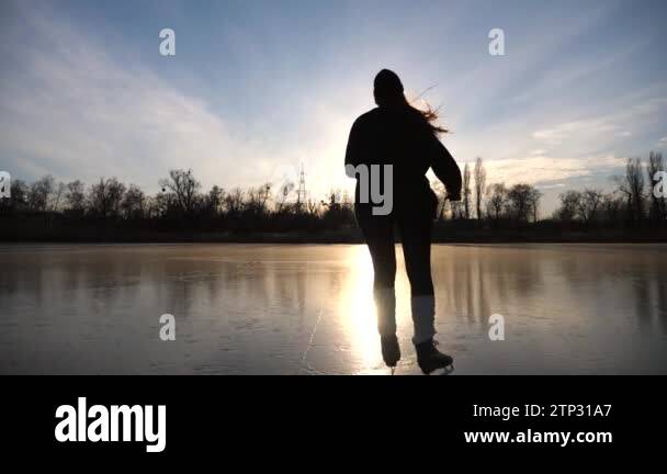 Young woman is skating on ice. Girl training alone at frozen lake or ...