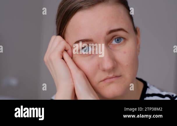 Close-up of a sad, pensive young woman sitting alone, thinking about ...