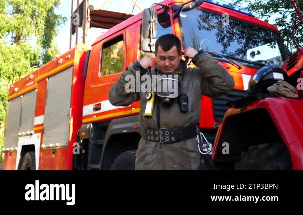 Young fireman in uniform taking off oxygen mask stands near a fire ...