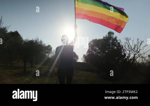 Young woman alone with LGBTQ+ flag walking as it waves in the sunset ...