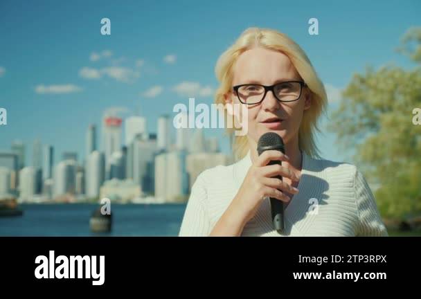 A woman journalist and TV presenter speaks into a microphone on a city ...