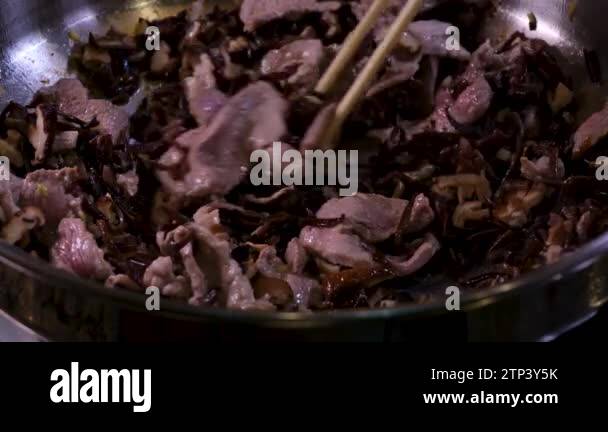 adding chopped garlic and ginger to beef in a frying pan frying raw ...