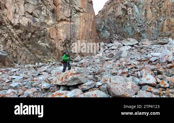 A man with a large backpack and trekking poles walks in the mountains ...