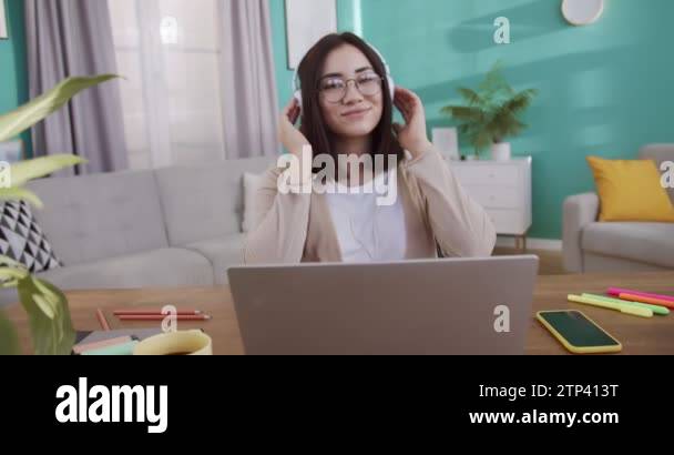 Woman listening to music using earphones sitting next to sofa in room ...