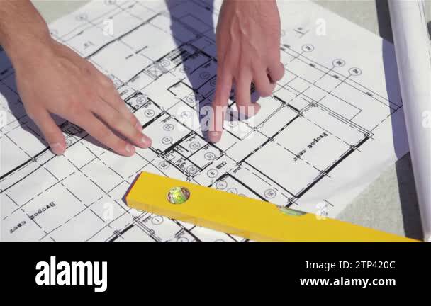 Close up of male fingers pointing at the plan of the building under construction. Two men ...