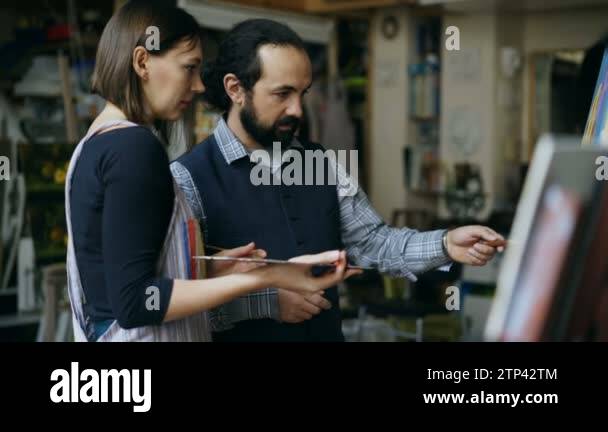 Skilled artist man teaching young girl to draw paintings and explaining ...