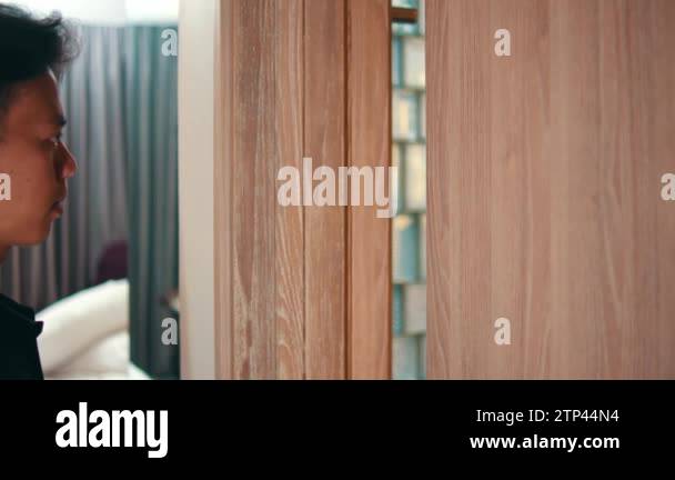 an Asian man is spying on his girlfriend while in the bathroom of a hotel room at night Stock ...