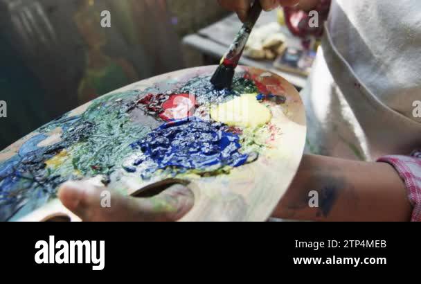Hands of biracial female artist mixing paints on palette using brush in ...