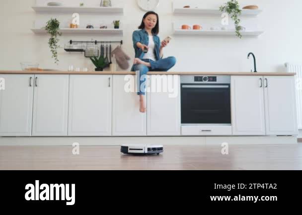 Beautiful asian woman plugging robot vacuum cleaner via wireless remote ...