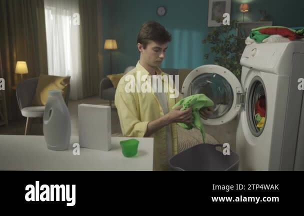 Dark-haired man standing next to a washing machine, unloading clothes ...
