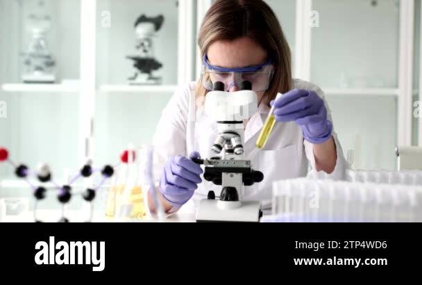 Lady scientist examines sample under microscope holding flask with ...
