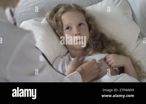 Sick kid lying in bed and crying while doctor examining her with ...