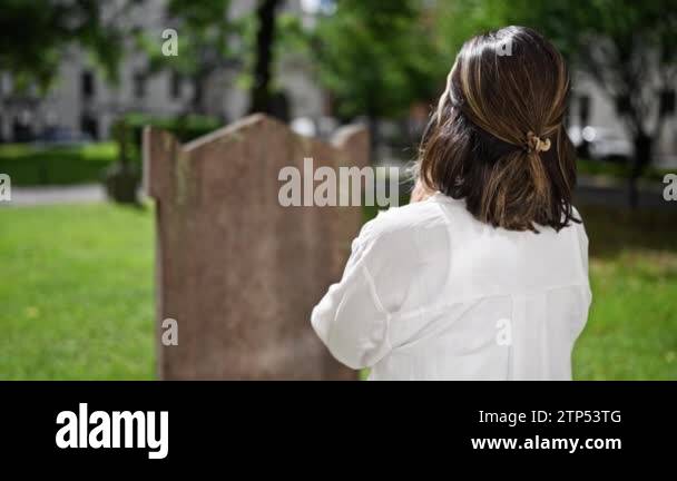 Beautiful young hispanic woman praying and mourning by tombstone at ...