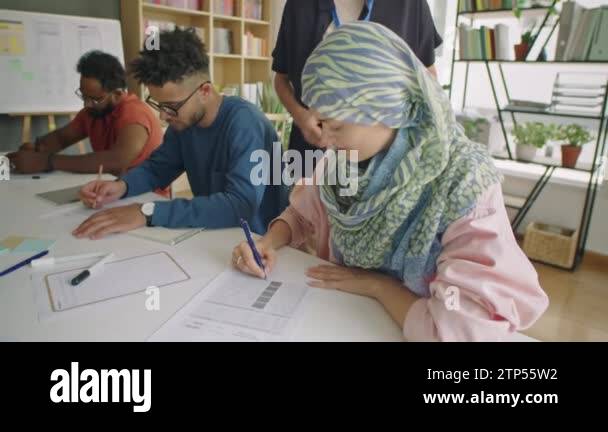 Female teacher helping young muslim girl in hijab during exam in ...