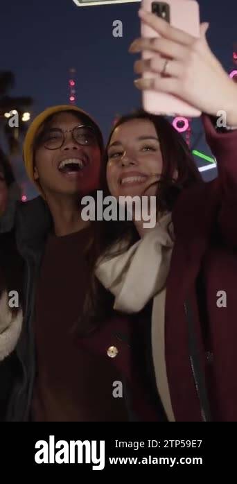 Vertical. Young girl and her group of friends making a video call from the amusement park. Four ...