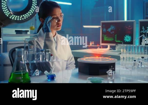 Medium-sized video capturing an asian female scientist wearing glasses and a lab coat sitting in ...