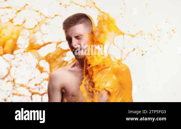 Young shirtless man being covered with thick yellow paint against white ...