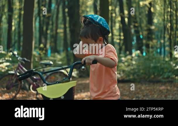 A boy child puts on a helmet and rides a bicycle in the park. Happy ...