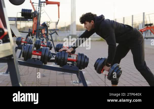 Determined Man at Street Gym Pushes himself while Using a Dumbbell ...