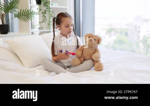 Smiling girl using toy syringe for injecting fluffy teddy bear with ...