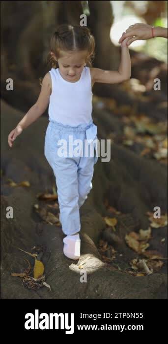 Cute little girl walking on the tree roots in the park holding her ...