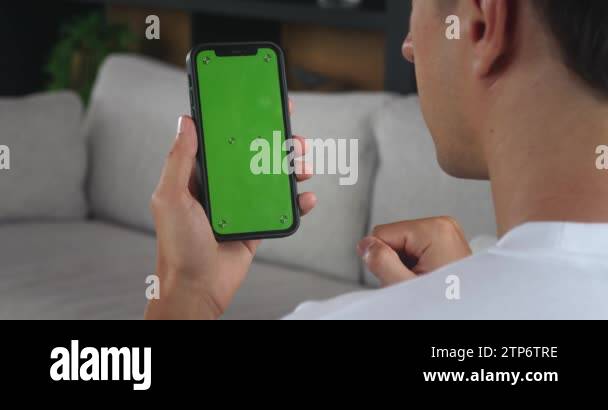 Unrecognizable man tapping and swiping on green screen, using phone indoor at home office. Over ...
