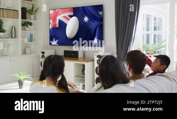 Asian family watching tv with rugby ball on flag of australia on screen ...