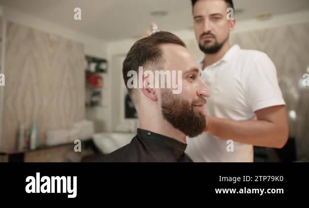 Attractive male is getting a modern haircut in barber shop. Barber sets ...