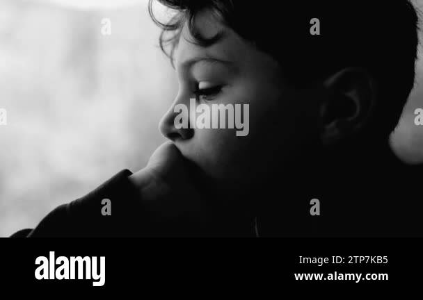 Somber look of child sitting by train window looking out at view with ...