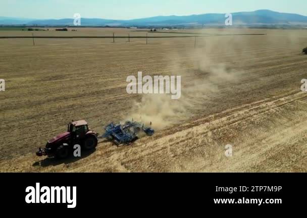 Flying over tractor with harrow system plowing ground on cultivated ...