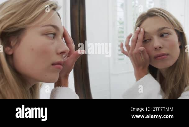 Biracial woman touching her face looking in mirror in bathroom, slow ...