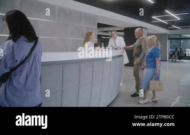 Elderly couple come to reception desk in clinic lobby and make ...