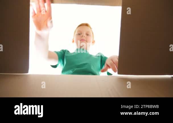 Small red-haired boy looking in parcel box with positive emotions and ...
