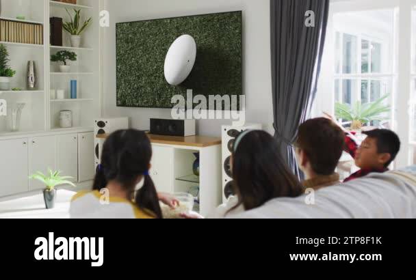 Asian family watching tv with rugby ball at stadium on screen ...