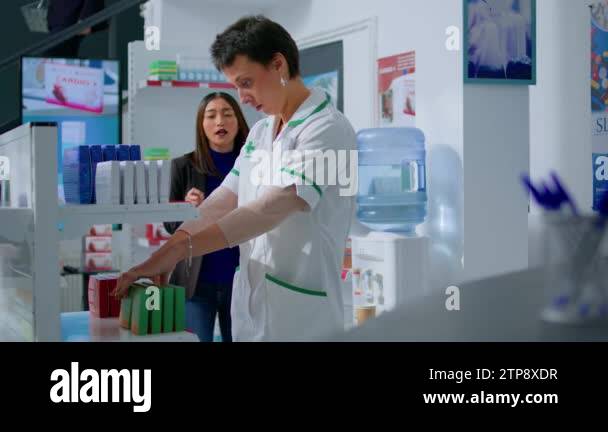 Asian woman in pharmacy looking at digital advertising on TV screen ...